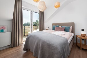 Quarto com uma cama grande, mesa de cabeceira, janela com cortinas e vista para o exterior.