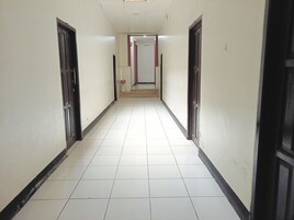 Um corredor comprido e estreito com pisos e paredes de azulejos brancos, com portas escuras de cada lado.