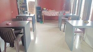 Uma área de refeições com mesas e cadeiras, geladeira e uma janela com cortinas.