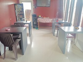 Uma área de refeições com mesas e cadeiras, geladeira e uma janela com cortinas.