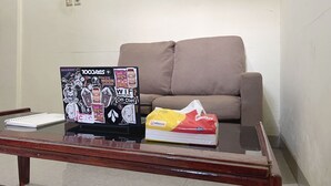 Uma sala de estar com um sofá marrom, uma mesa de centro de vidro com um caderno, um jogo de tabuleiro e um pacote de lenços.