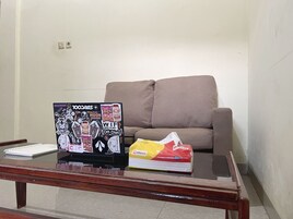 Uma sala de estar com um sofá marrom, uma mesa de centro de vidro com um caderno, um jogo de tabuleiro e um pacote de lenços.