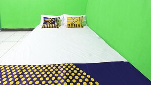 Cama com lençóis brancos, duas almofadas com estampas azuis e amarelas, e manta com bolinhas azuis e amarelas.