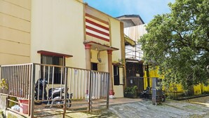 Um edifício com fachada amarela, portão de metal e uma árvore em primeiro plano.