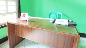 Uma mesa de madeira com tampo de vidro, uma cadeira verde e uma placa branca com texto vermelho.