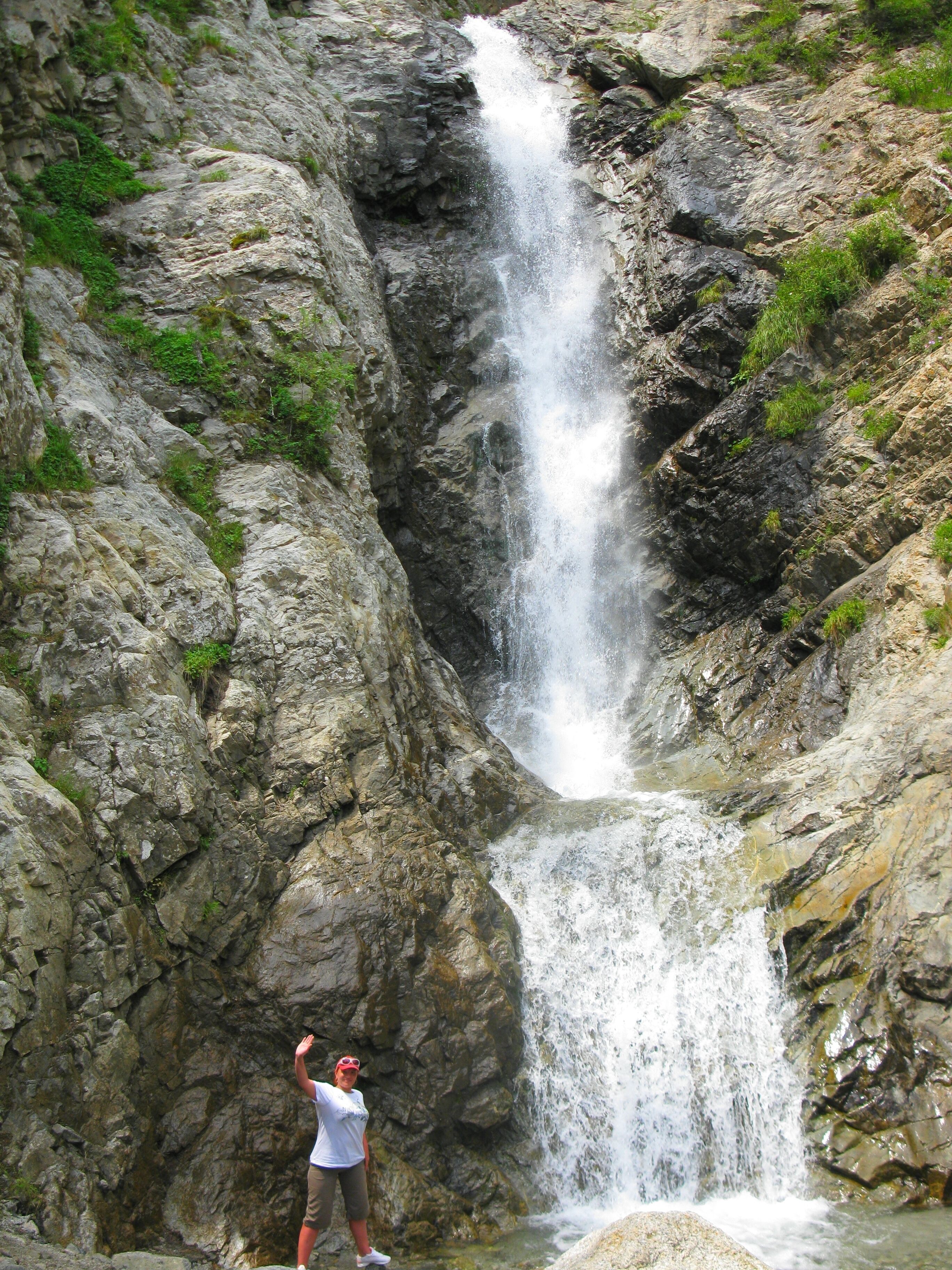 Uma cascata despencando por um penhasco rochoso, com uma pessoa em pé na base.