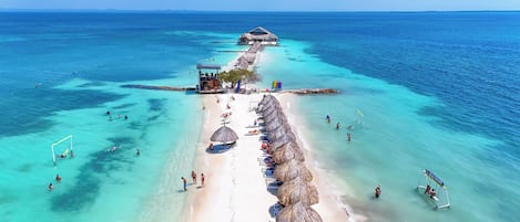 Um resort à beira-mar com um píer comprido que leva a bangalôs sobre a água, águas turquesa cristalinas e uma praia arenosa.
