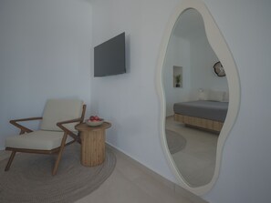 Quarto moderno com cama, uma cadeira, uma mesinha de centro com frutas e uma televisão fixada na parede.