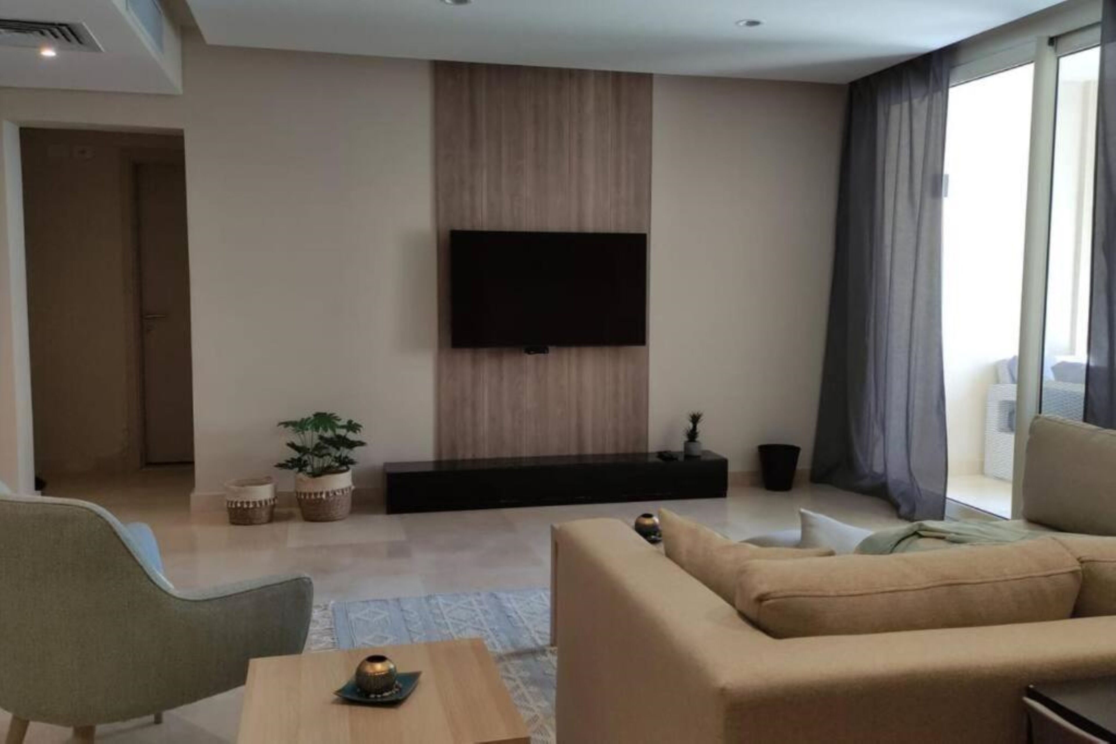 Uma sala de estar moderna com uma televisão de tela plana na parede, um sofá, uma mesa de centro e um vaso de plantas.