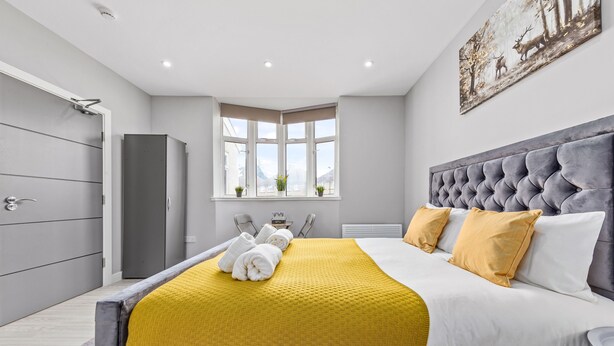 Quarto moderno com cama grande, cabeceira cinzenta e janela com vista.