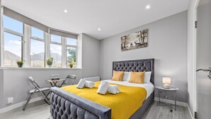 Quarto moderno com cama grande, escrivaninha e cadeira, janela com plantas e um quadro na parede.