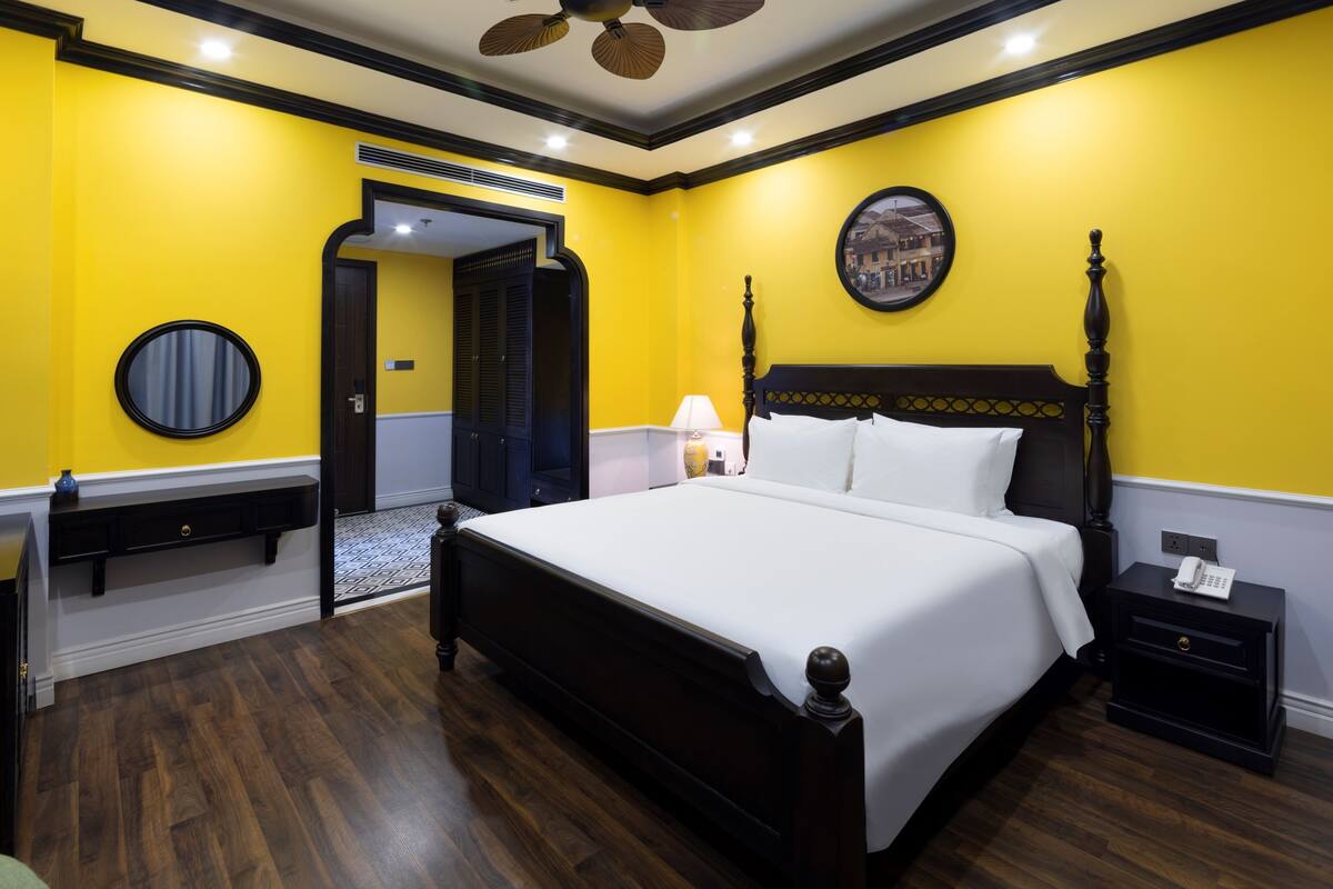 Quarto com uma cama grande, um ventilador de teto, mesa de cabeceira com abajur, criado-mudo, espelho e guarda-roupa.