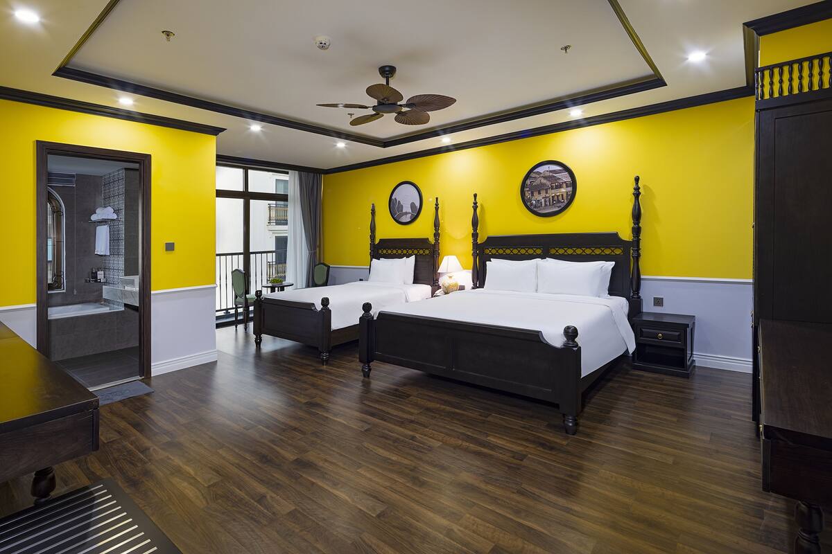 Quarto de hotel com duas camas, ventoinha no teto e vista para o exterior.