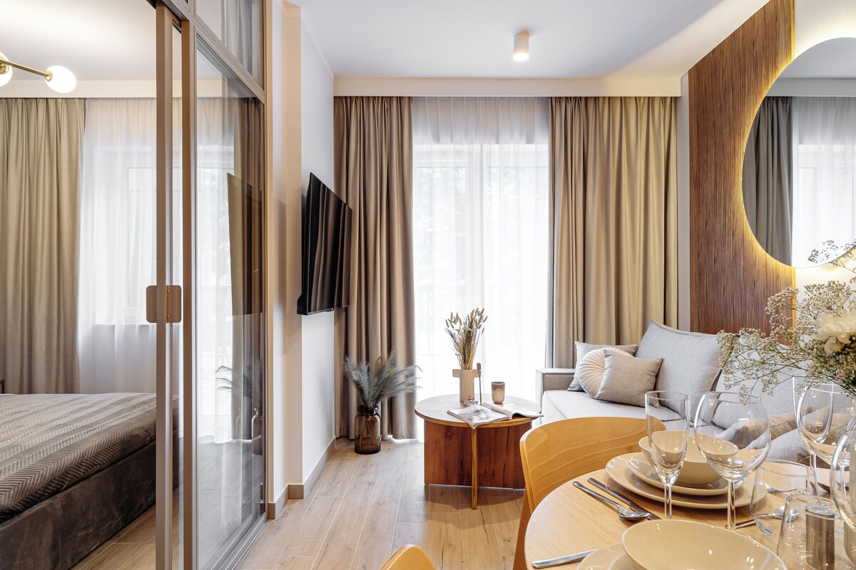 Quarto de hotel moderno com uma cama grande, uma área de refeições com uma mesa redonda e um espaço de estar com um sofá.