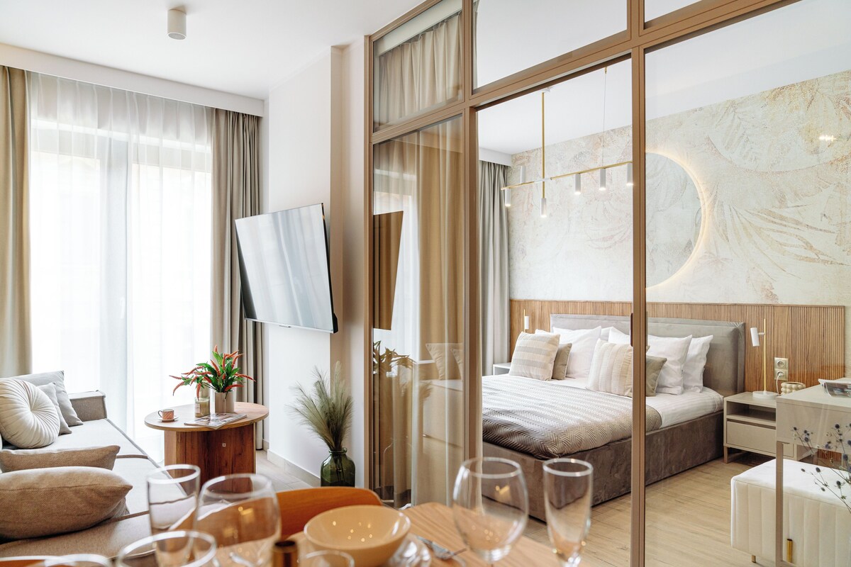 Quarto de hotel moderno com uma cama grande, área de estar com mesa e televisão fixada na parede.