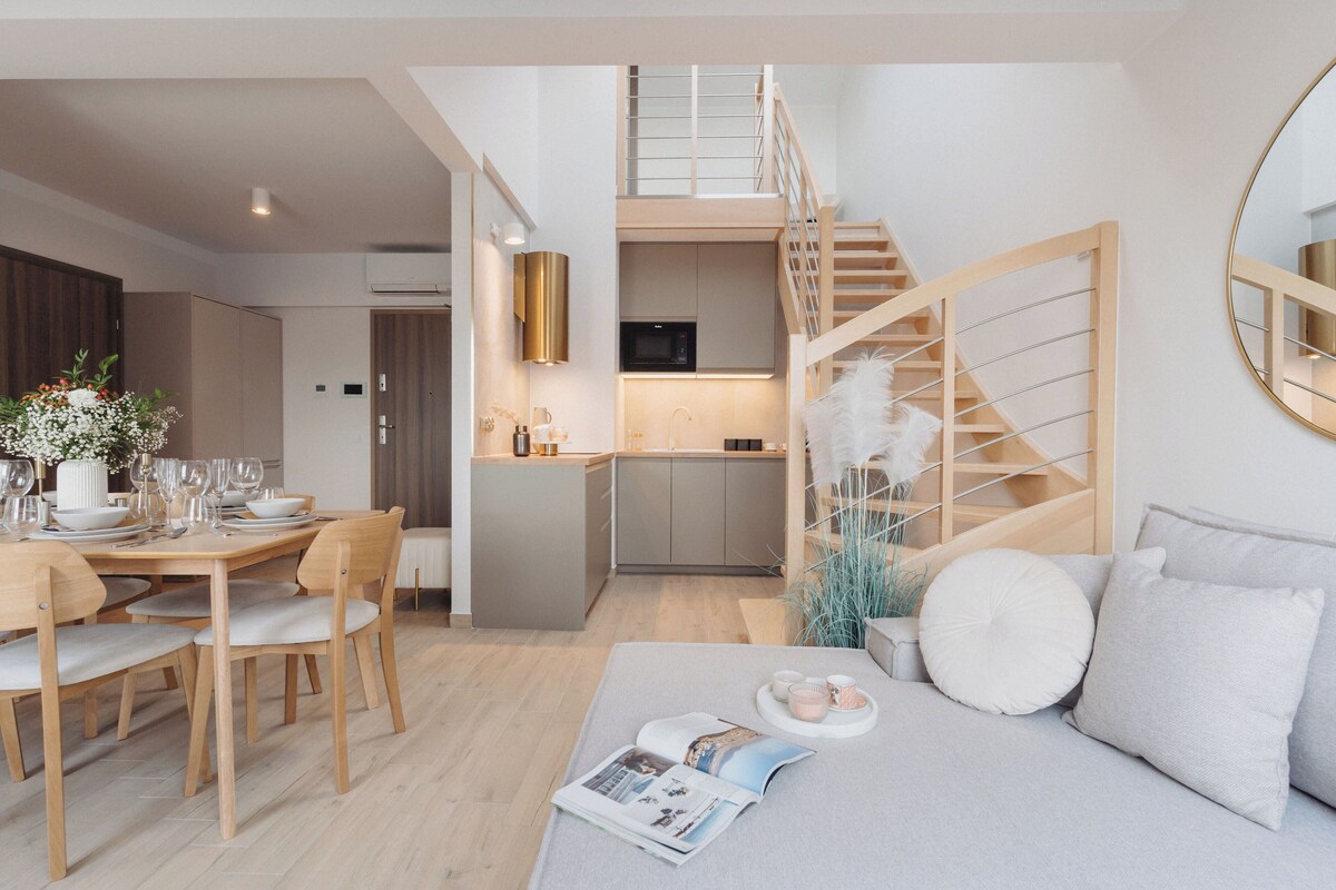 Um apartamento moderno com área de jantar, cozinha, escada e sala de estar com sofá e uma revista.
