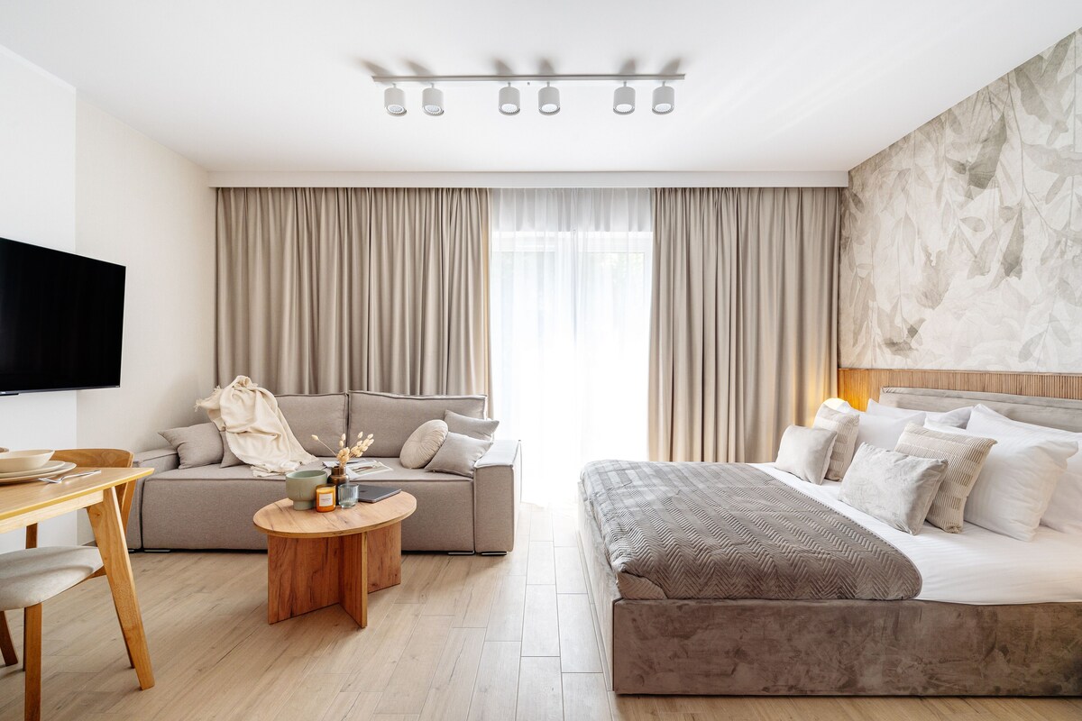 Quarto de hotel moderno com uma cama grande, um sofá, uma mesa de jantar e uma televisão.