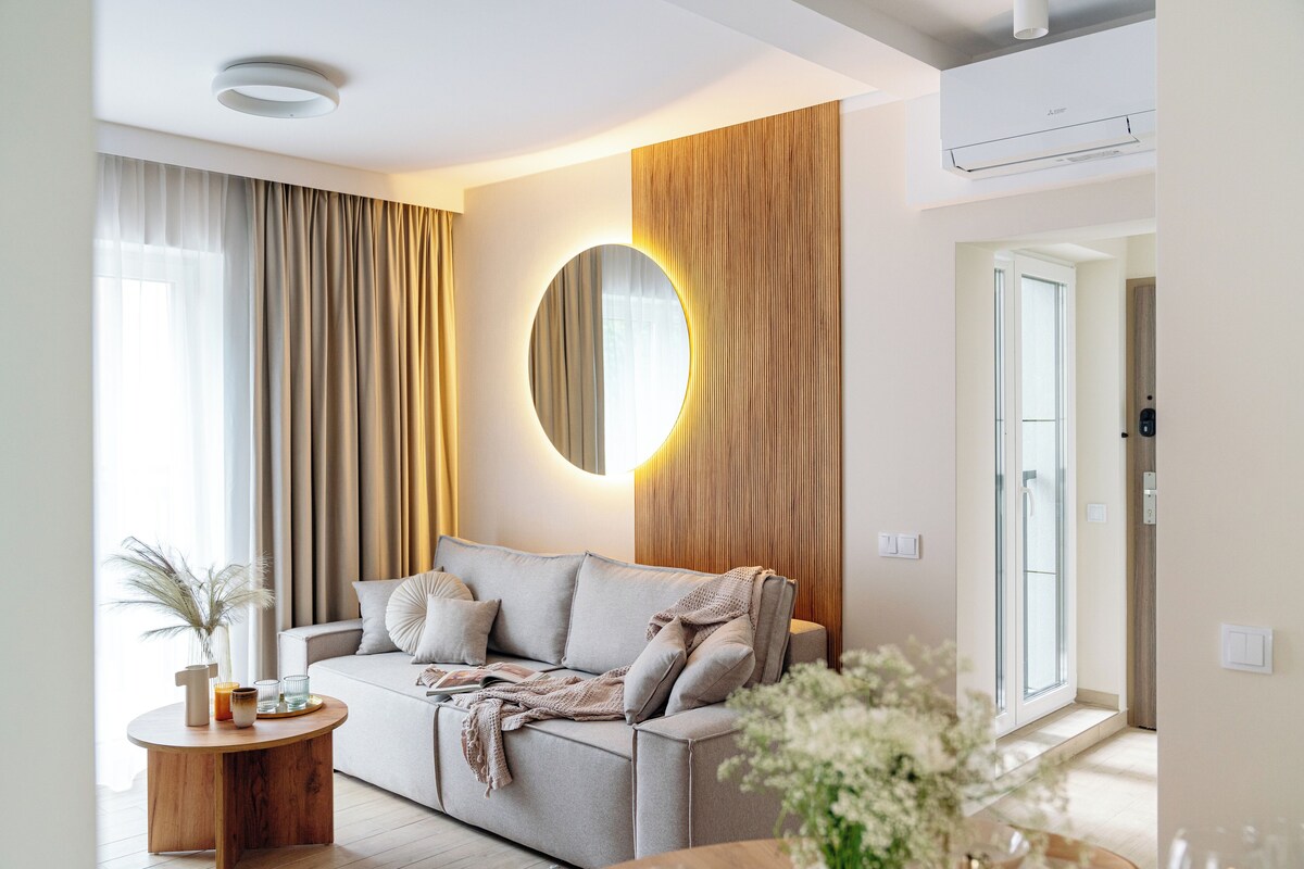 Uma sala de estar moderna com um sofá, um espelho redondo e uma pequena mesa de madeira.