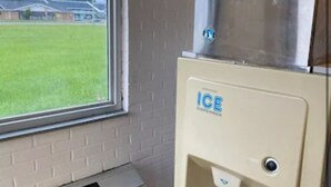 Quarto com janela, ar condicionado fixado na parede e dispensador de gelo branco.