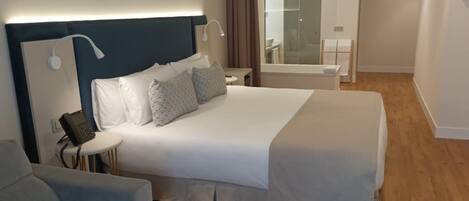 Quarto de hotel moderno com uma cama grande, mesas de cabeceira, telefone e um espaço de estar.