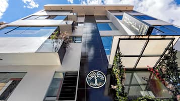 Um edifício moderno com um logotipo, janelas amplas e uma varanda com plantas.