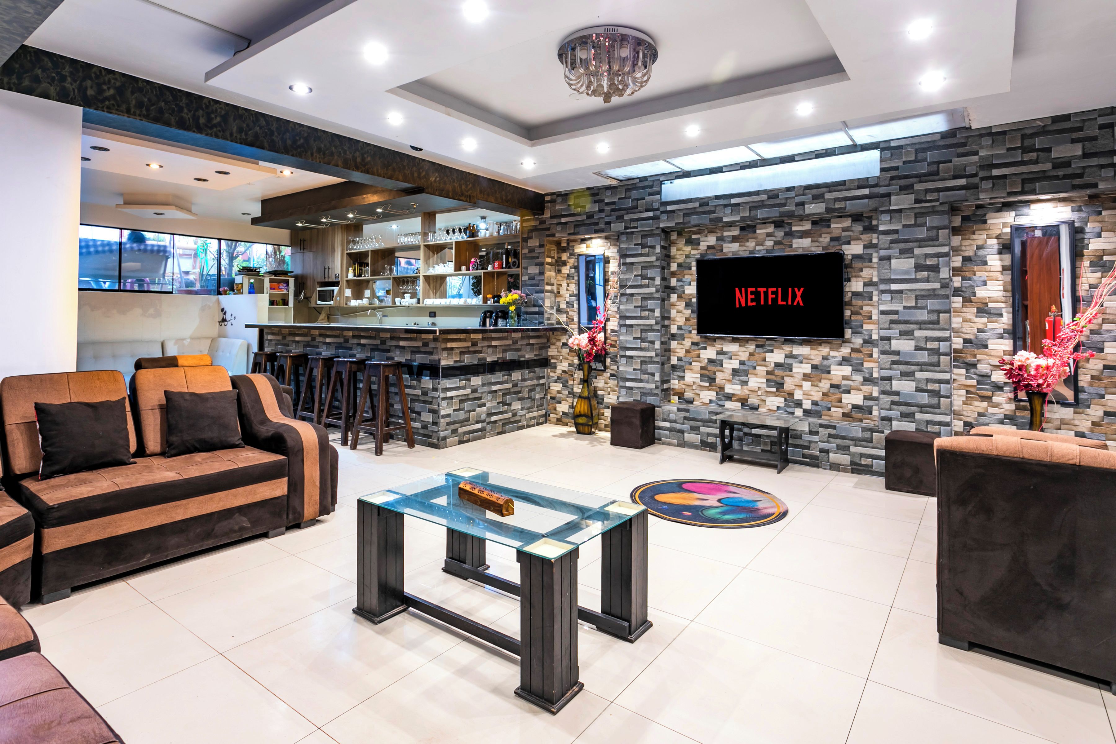 Uma sala de estar moderna com balcão de bar, sofás, mesa de centro e uma tela de TV exibindo 'NETFLIX'.