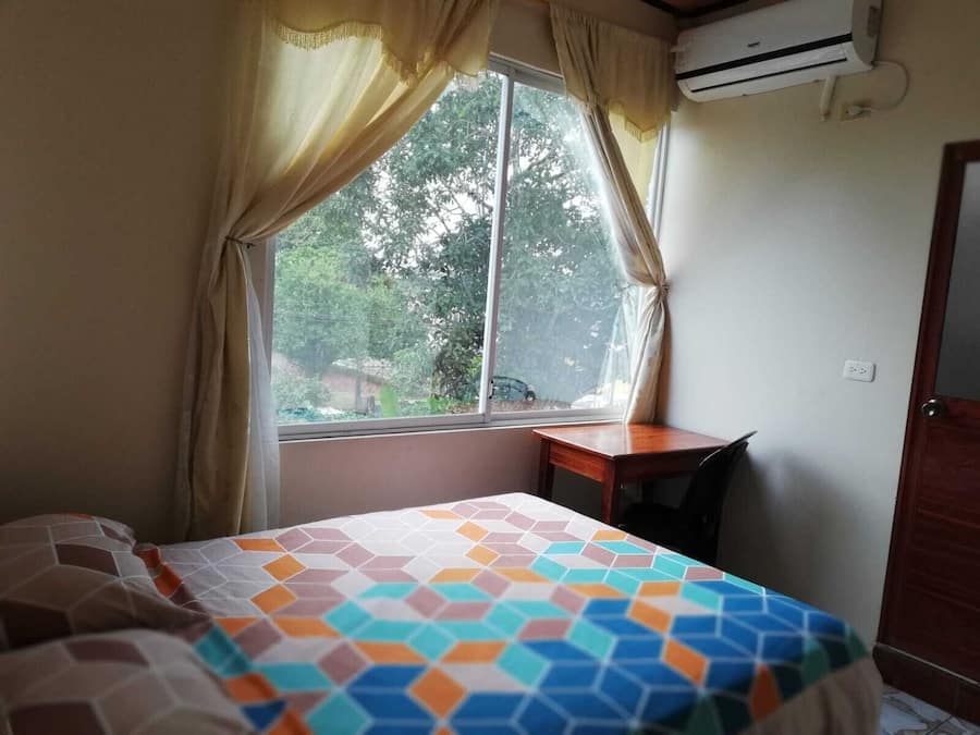Quarto com cama, escrivaninha e janela com cortinas.