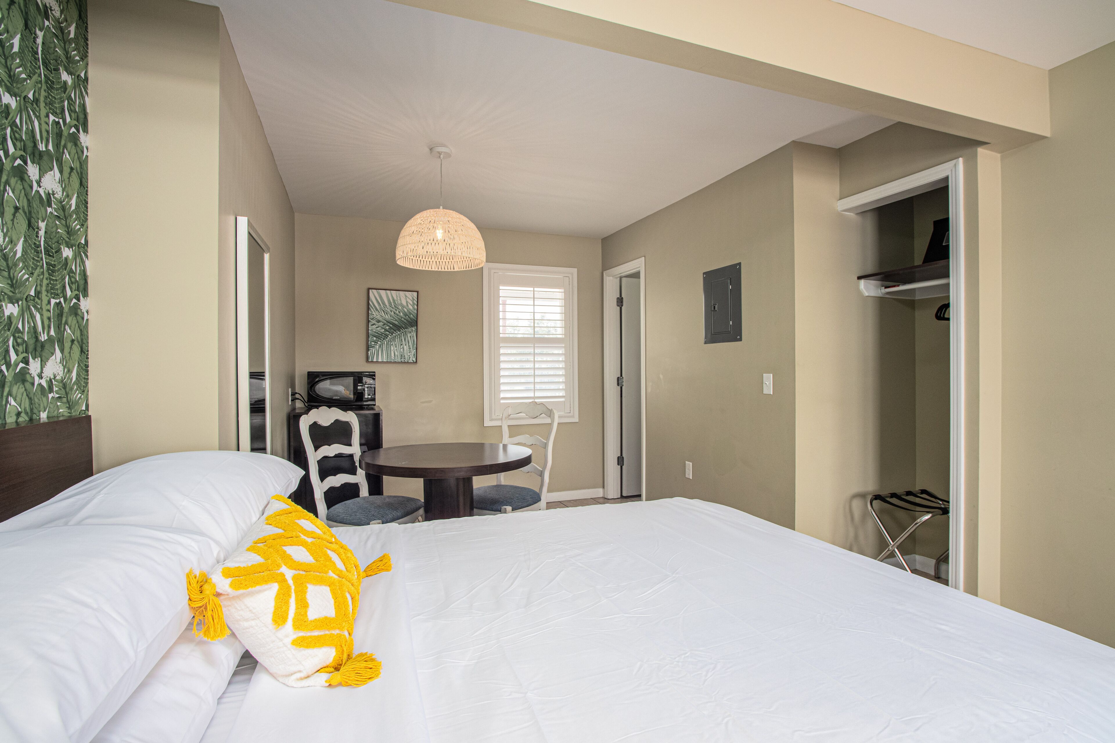 Quarto de hotel com uma cama grande, uma mesa de jantar com cadeiras, uma pequena cozinha e um closet espaçoso.