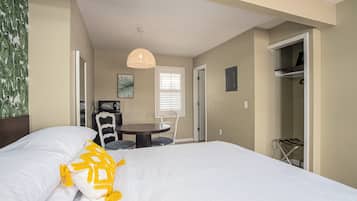 Quarto de hotel com uma cama grande, uma mesa de jantar com cadeiras, uma pequena cozinha e um closet espaçoso.