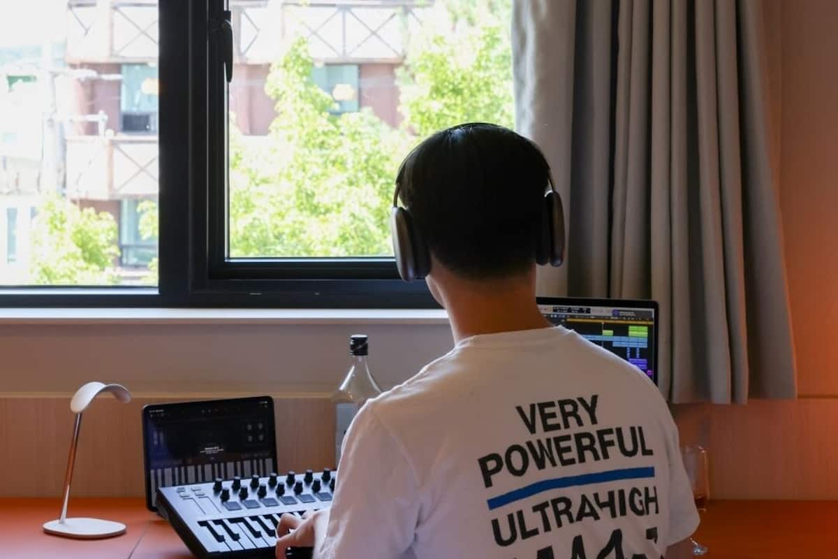Uma pessoa sentada em uma mesa com equipamento de produção musical, incluindo um teclado e um monitor de computador.