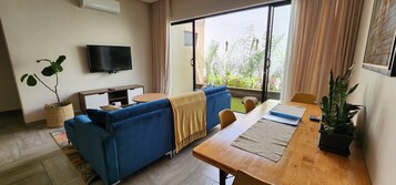 Uma sala de estar moderna com um sofá azul, uma mesa de jantar de madeira e uma TV na parede.