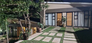 Uma casa moderna com área de jardim pavimentada, janelas amplas e plantas em vasos.