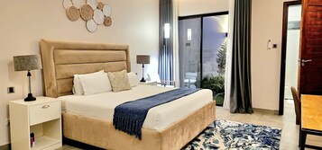 Um quarto com uma cama grande, luminárias de cabeceira, mesa de cabeceira, tapete estampado e vista para o exterior por uma porta de correr.