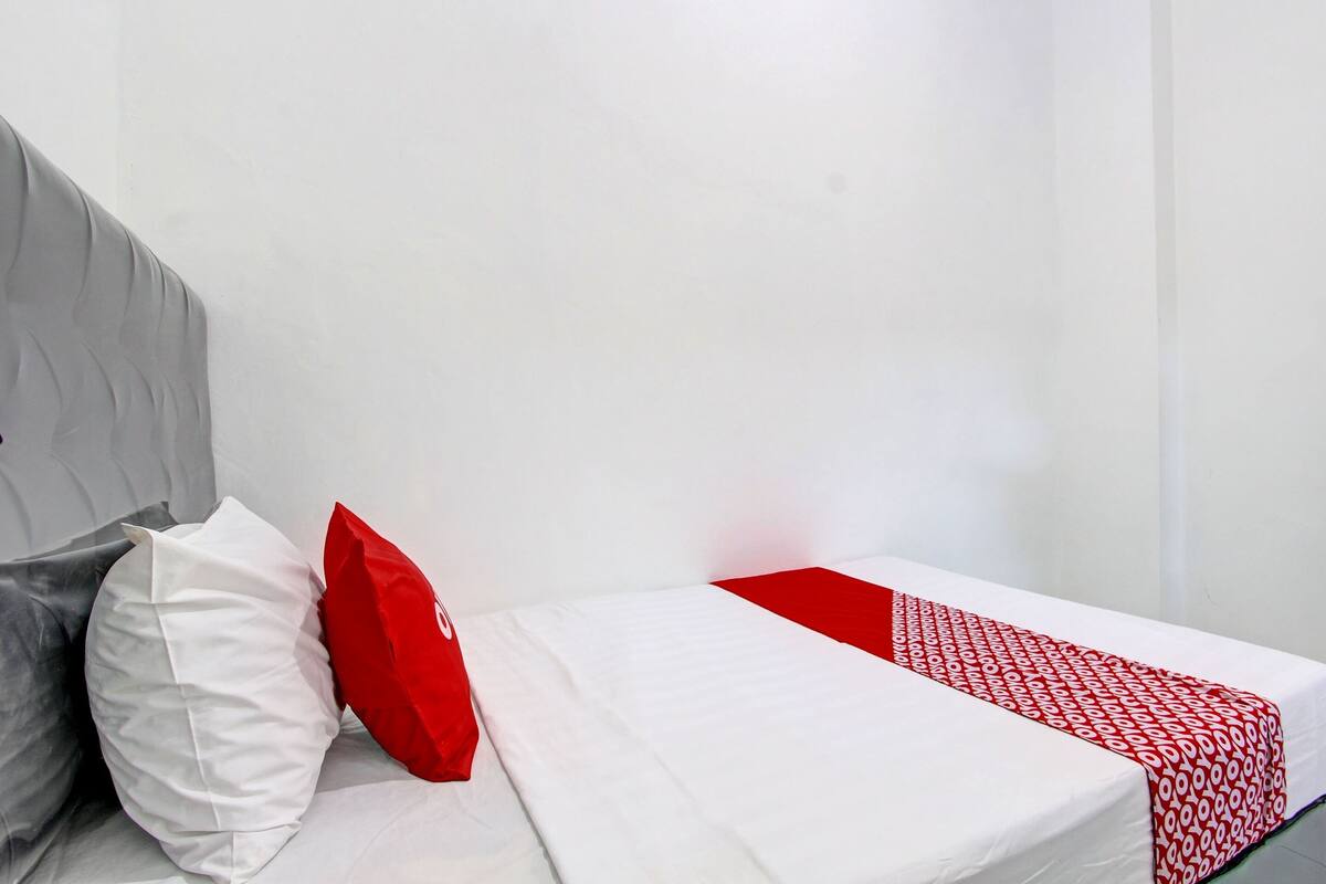 Cama com roupa de cama branca e vermelha, cabeceira cinza e almofada vermelha.