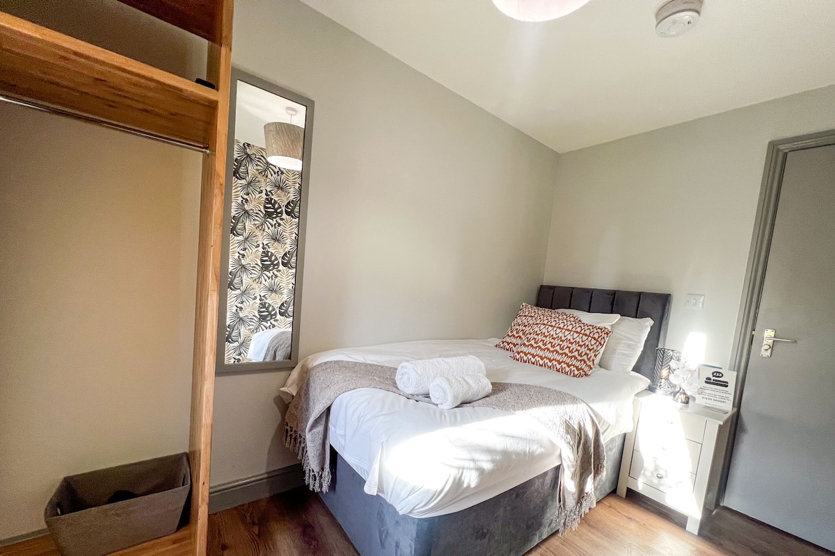Quarto com cama, mesa de cabeceira, espelho e chão de madeira.