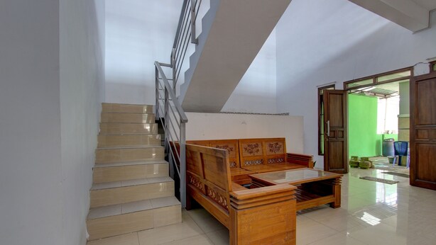 Uma escadaria com corrimão de madeira e uma cama de madeira com detalhes elaborados em um quarto com paredes brancas e uma tela verde ao fundo.