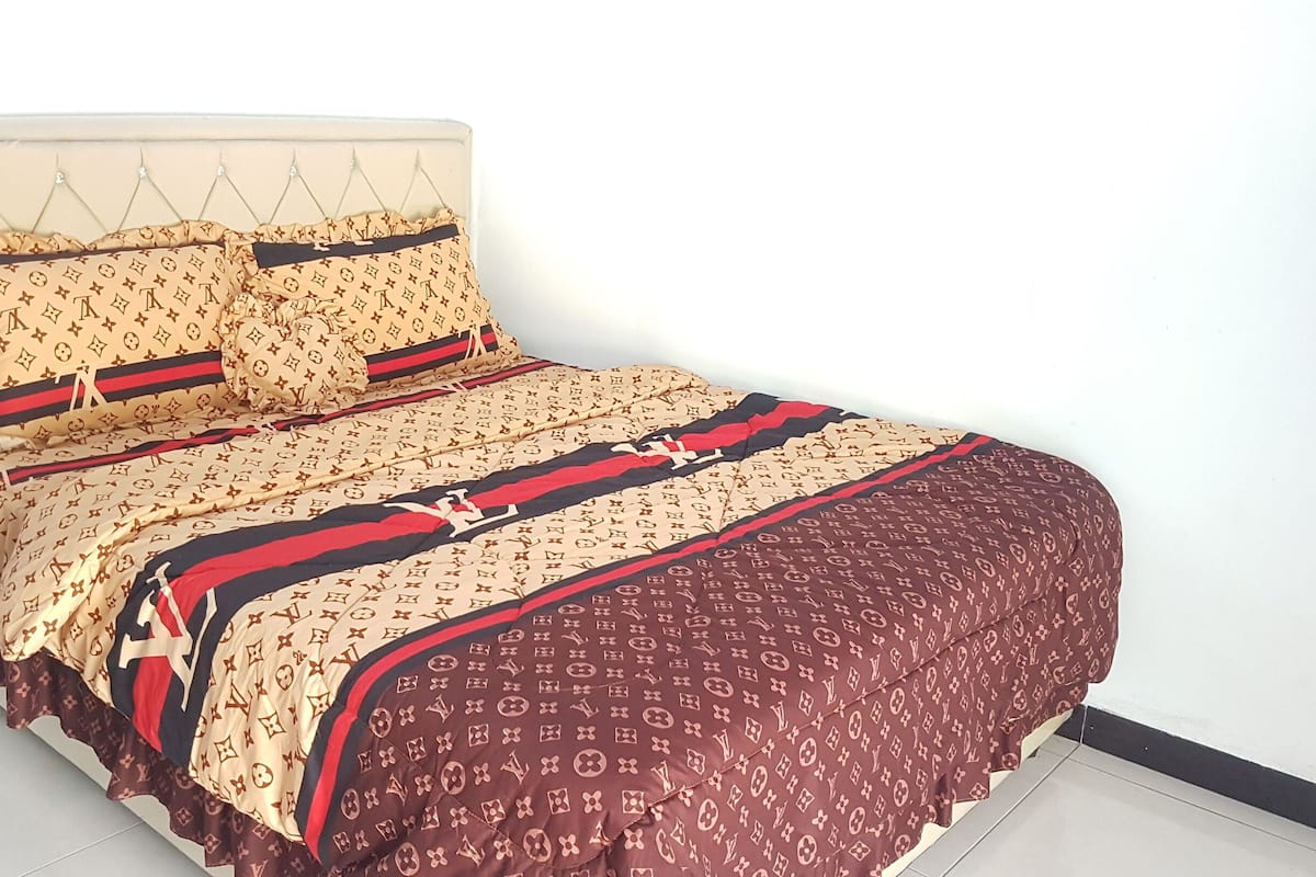Uma cama com colcha estampada e almofadas, uma cabeceira e uma parede lisa.