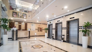 Um saguão de hotel com balcão de recepção, elevadores e um padrão decorativo no chão.