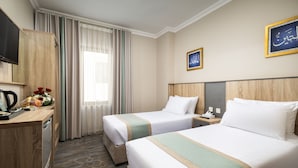 Quarto de hotel com duas camas, televisão, escrivaninha com cafeteira e janela com cortinas.