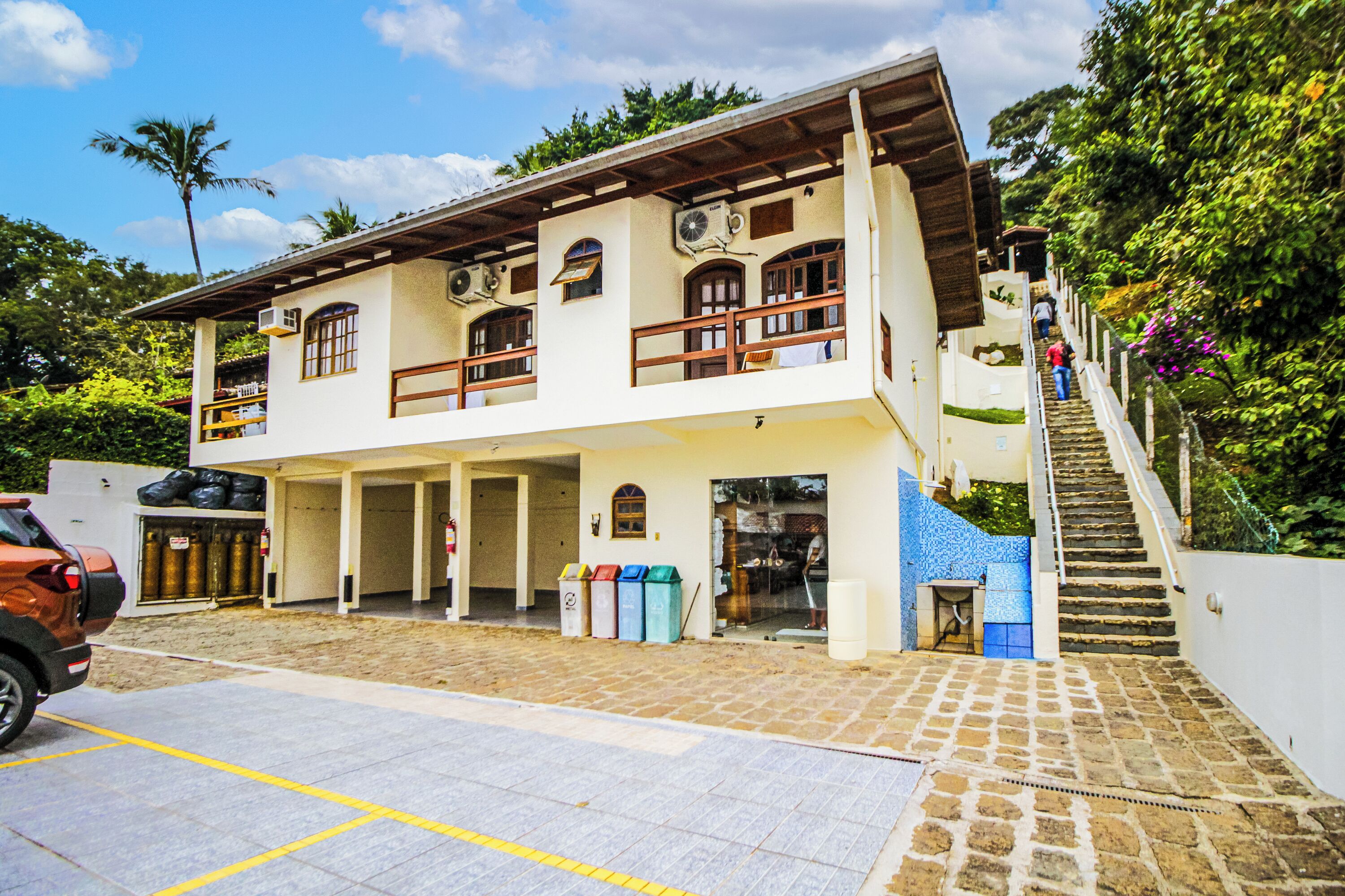 Um edifício de dois andares com entrada coberta, escadaria e área de estacionamento.
