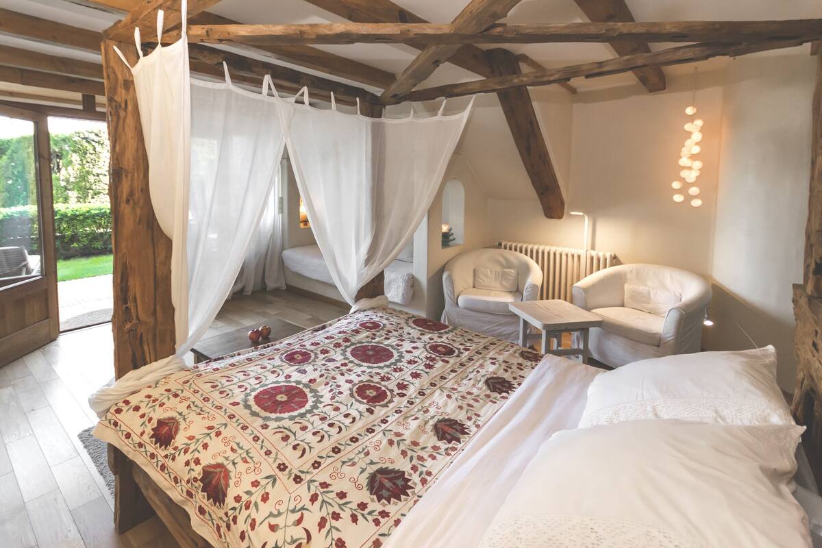 Quarto com uma cama grande, uma cadeira, uma mesa e uma janela com cortinas.