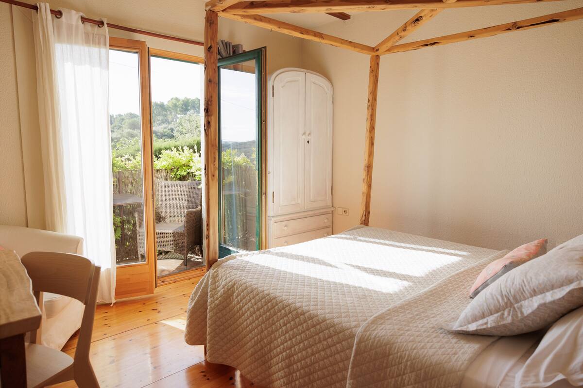 Quarto com cama, cadeira, guarda-roupa e porta de vidro deslizante para uma varanda.