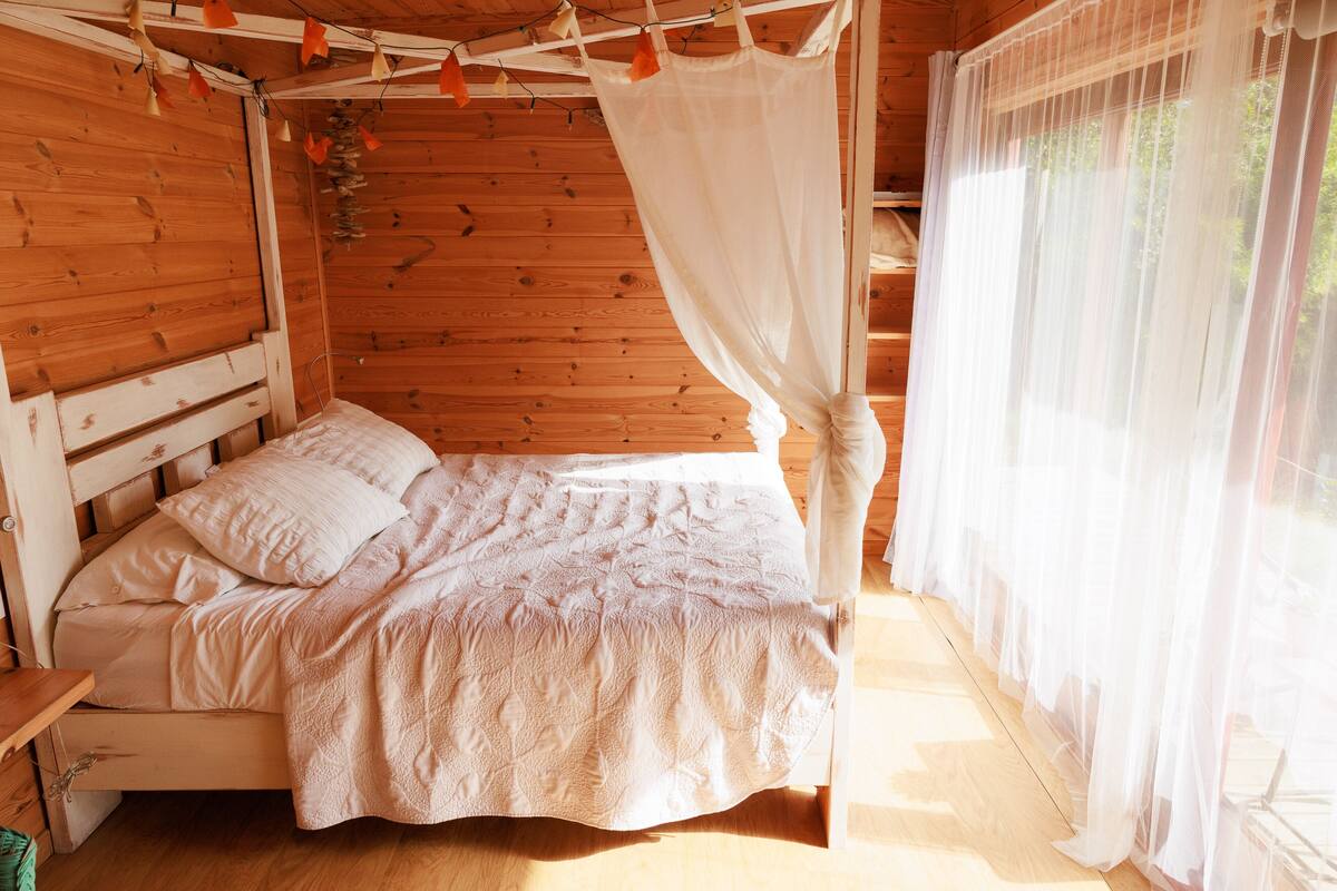 Quarto de cabana de madeira com cama, roupa de cama branca e um dossel.