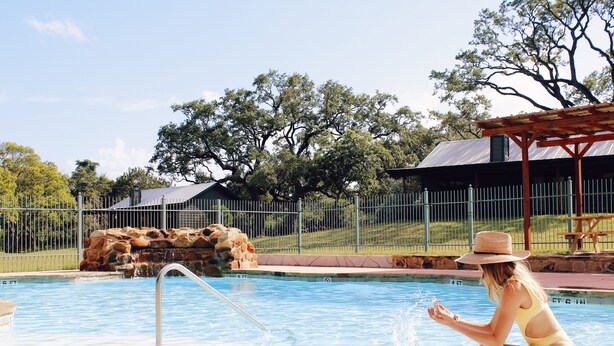 Piscina com elemento de pedra, escada de metal e pérgola de madeira.