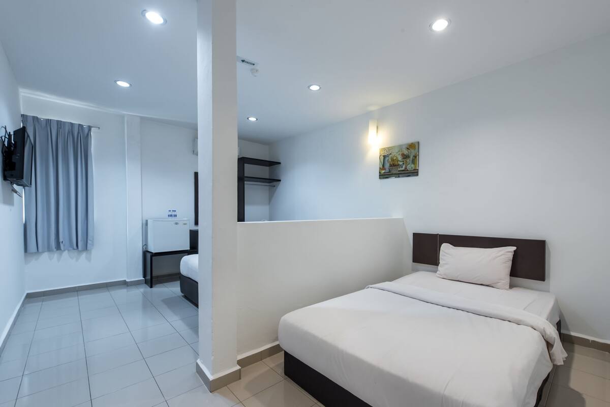 Quarto de hotel com cama, secretária, televisão e um quadro na parede.