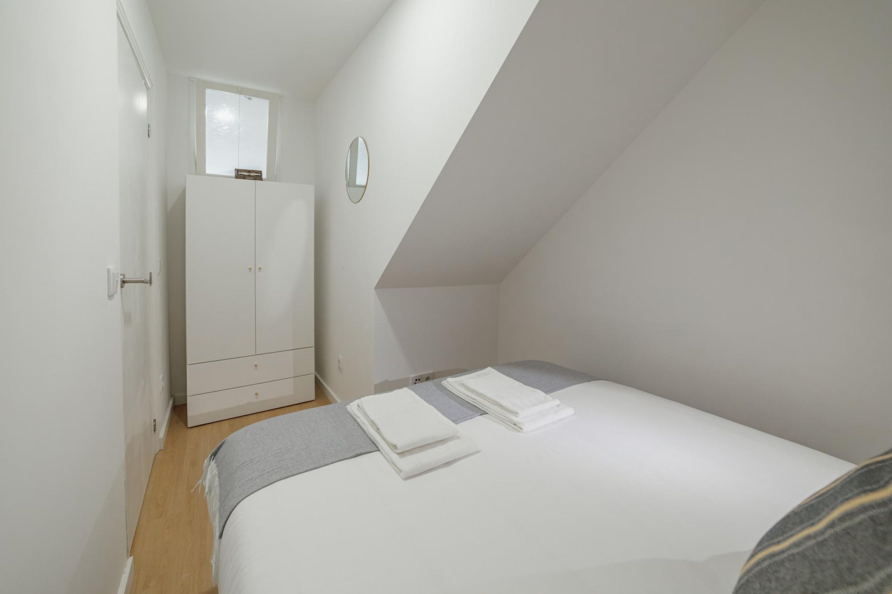 Quarto com cama, guarda-roupa, janela e espelho.