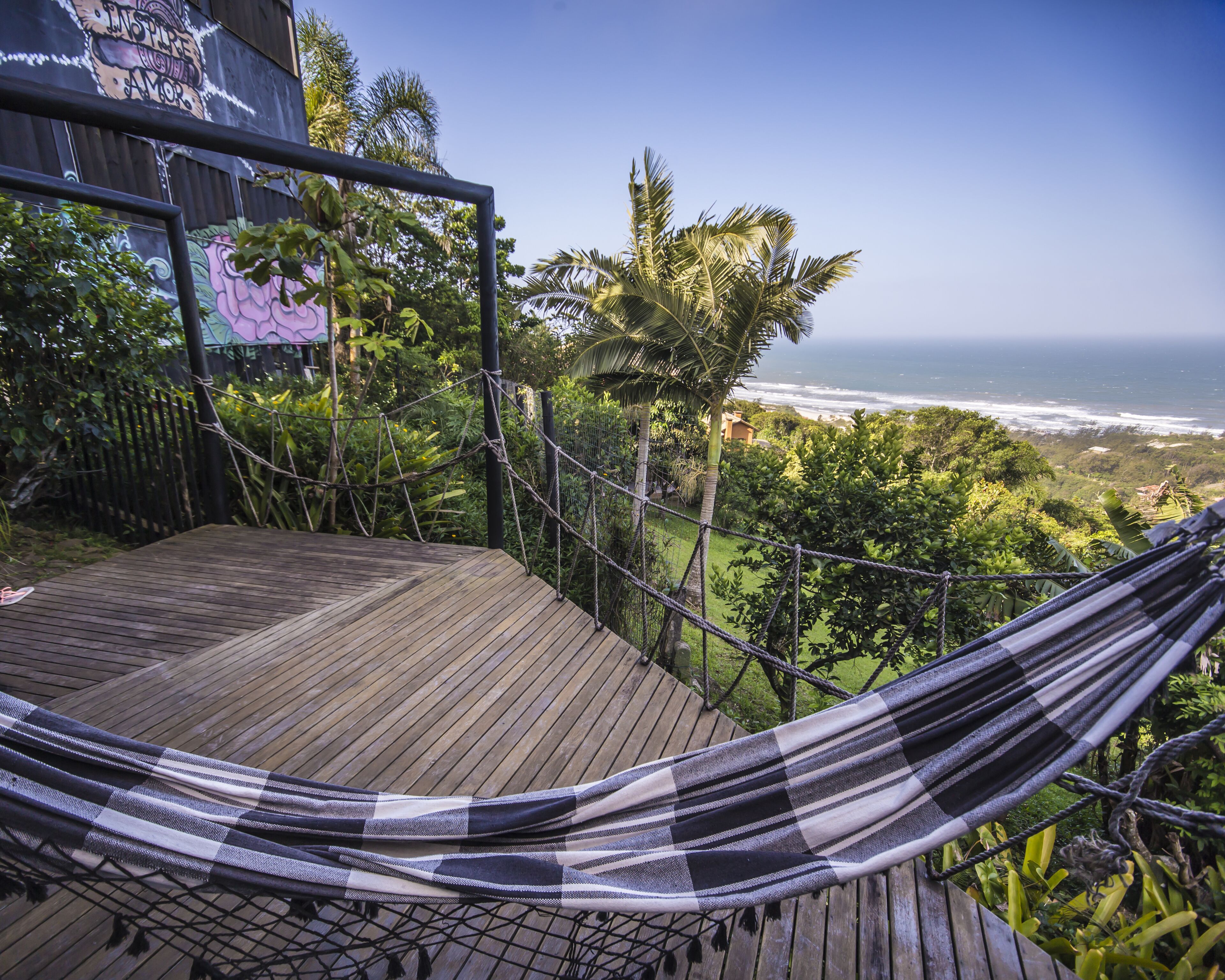 Uma rede em deck de madeira com vista para a costa e vegetação exuberante.