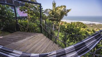 Uma rede em deck de madeira com vista para a costa e vegetação exuberante.