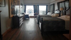 Quarto de hotel com duas camas, cómoda de madeira, secretária e uma janela grande com cortinas.