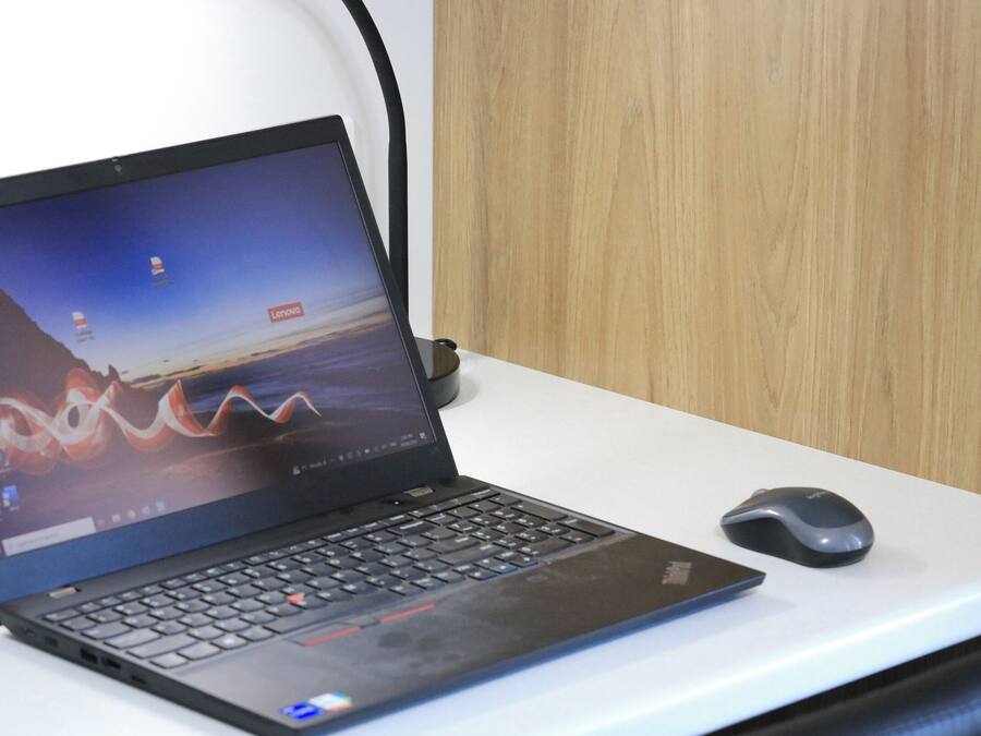 Um laptop sobre uma mesa branca, com um painel de madeira ao fundo.
